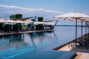 Piscina com espreguiçadeiras e guarda-sóis, rodeada por um jardim arborizado.