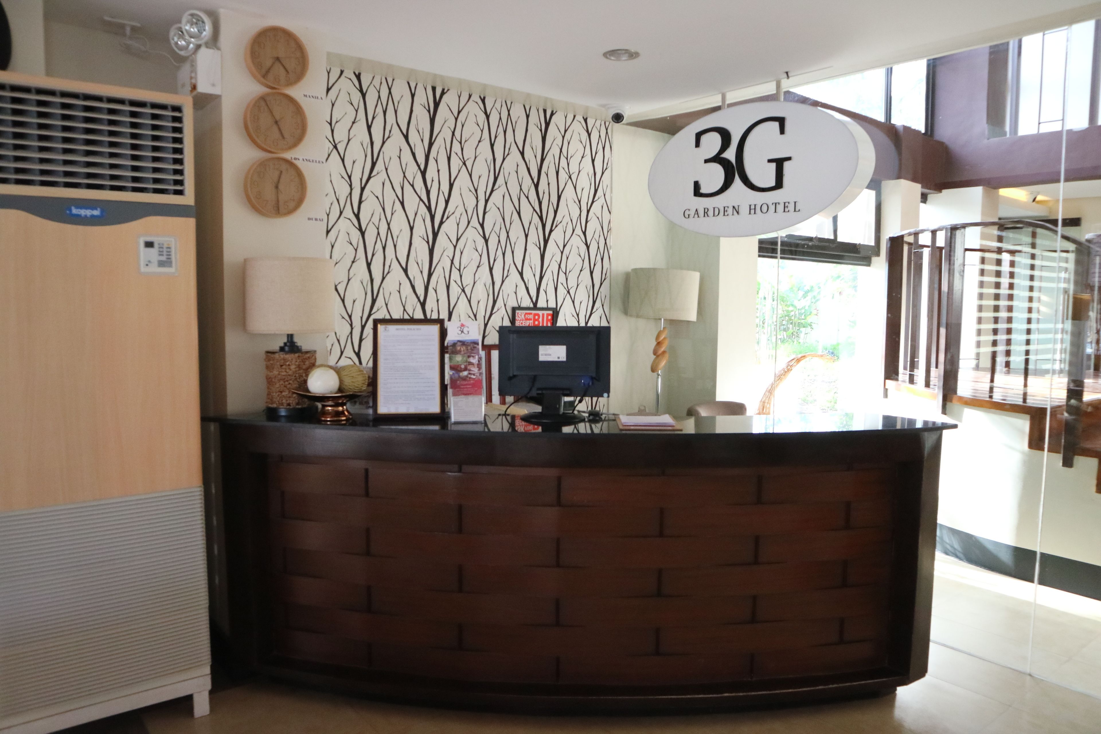 Uma receção com um ecrã digital, um relógio e uma placa a indicar o Garden Hotel.