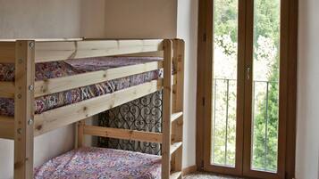 Uma cama beliche com roupa de cama estampada em um quarto com piso ladrilhado e uma porta para varanda.