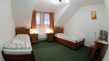 Quarto com duas camas de solteiro, uma pequena escrivaninha com televisão e uma janela com cortinas.