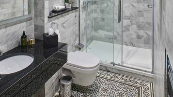 Um banheiro moderno com painel de backsplash de mármore, pia com bancada preta, vaso sanitário, chuveiro com box de vidro e piso com ladrilhos estampados.