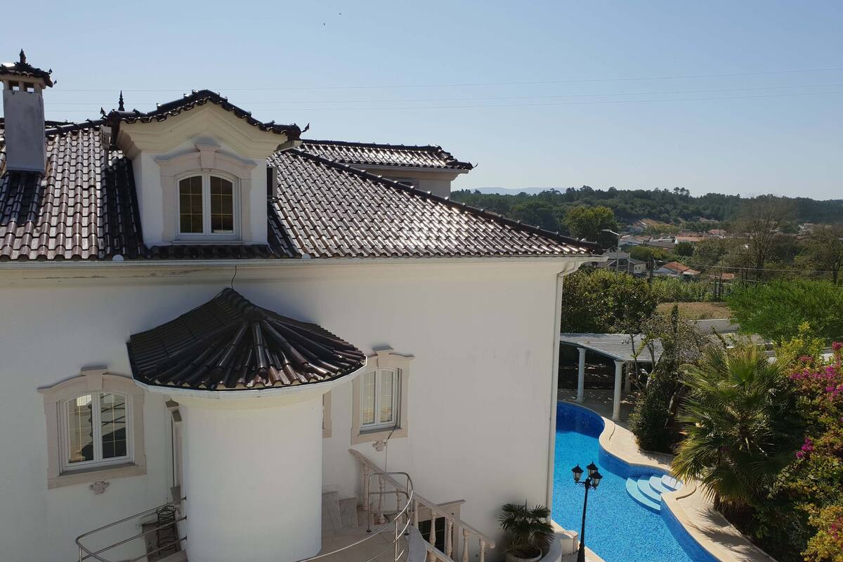 Um edifício grande com telhado em cerâmica, piscina e vista para uma área residencial.