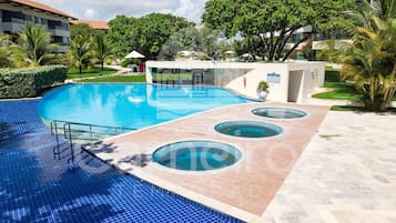 Piscina com deck revestido, cercada por vegetação e um edifício com design moderno.