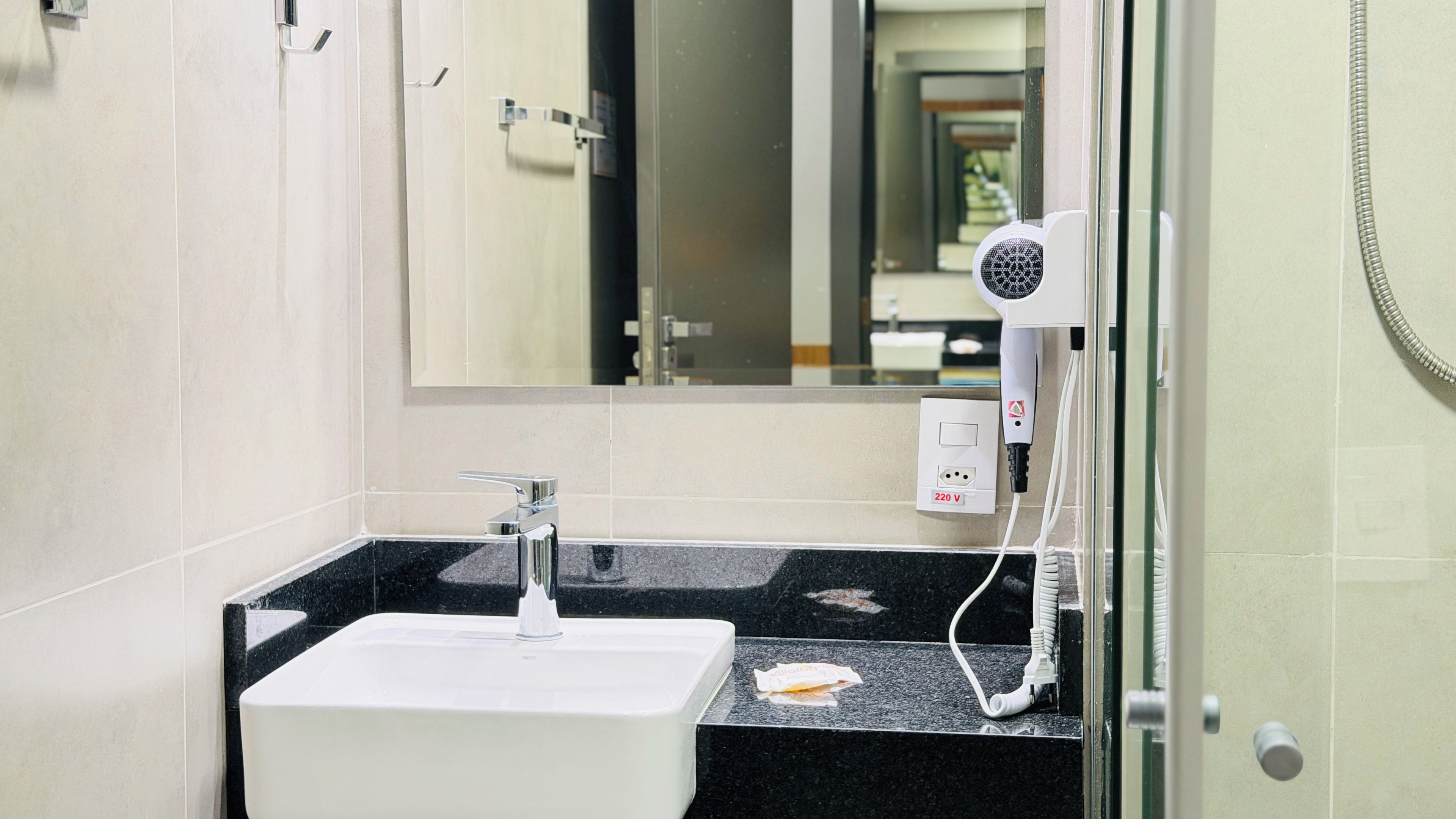 Casa de banho com lavatório branco, espelho e secador de cabelo ligado.