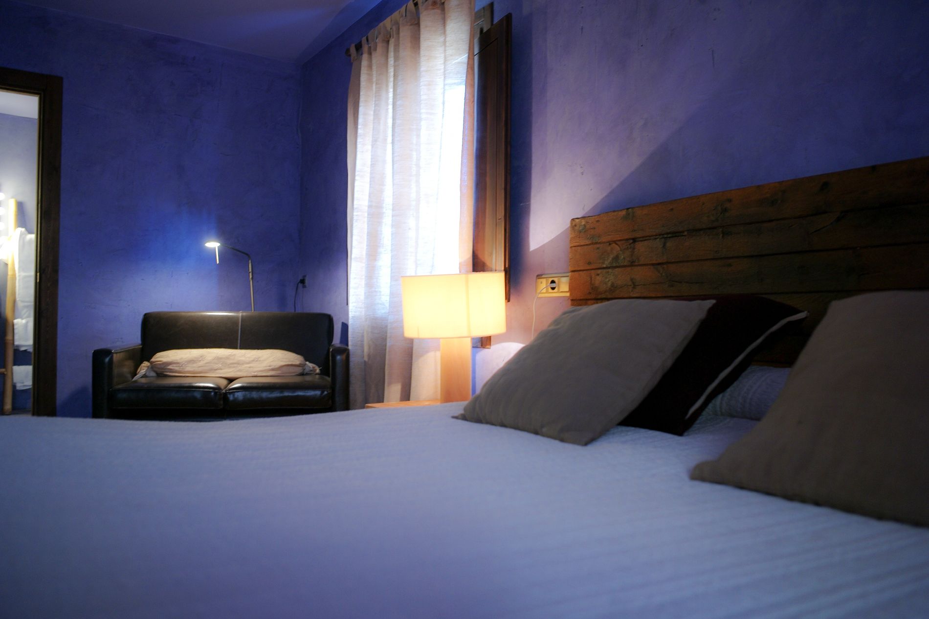 Quarto de hotel com cama, uma cadeira, uma luminária e cabeceira de madeira.