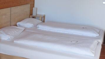 Cama com cabeceira de madeira e colchão branco, num quarto com chão de azulejos e parede de tijolos.