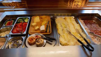 Buffet com diversos alimentos, incluindo presunto fatiado, queijo e legumes.