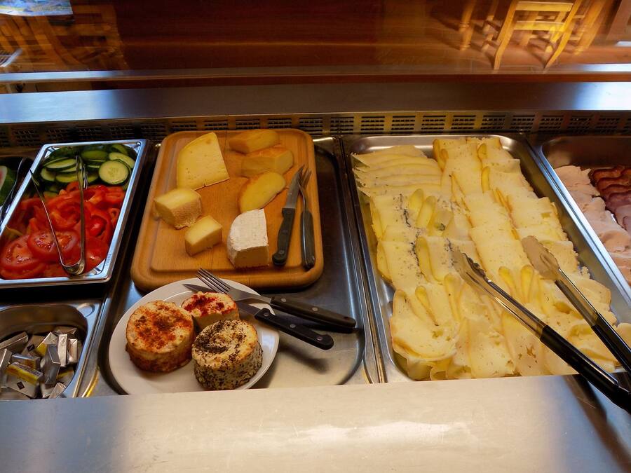 Buffet com diversos alimentos, incluindo presunto fatiado, queijo e legumes.