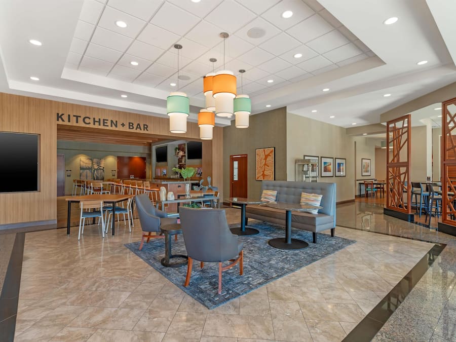 Um lobby de hotel moderno com cozinha, bar, áreas de estar e um teto decorativo.