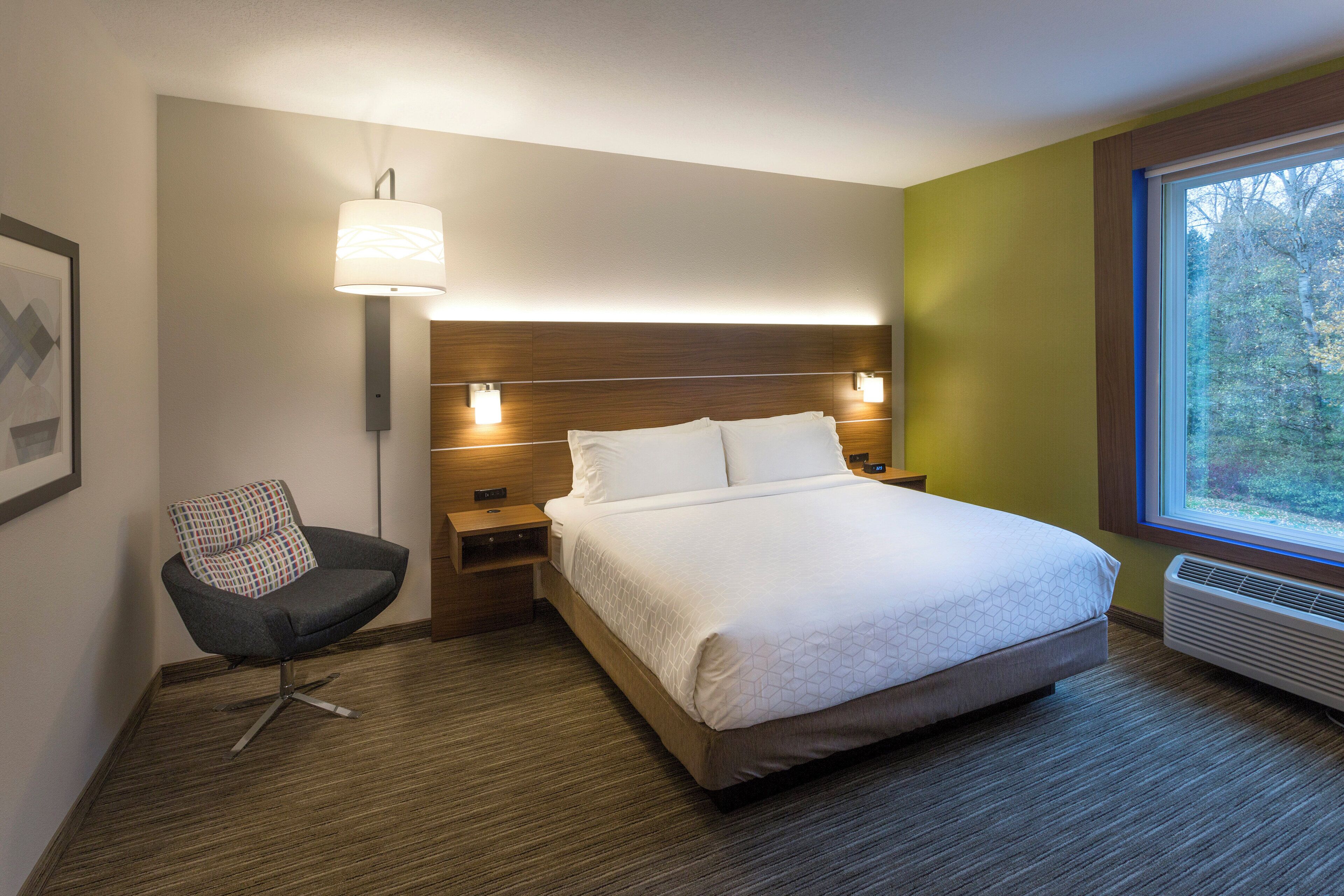 Quarto de hotel com cama, mesas de cabeceira, uma cadeira, abajur e janela.