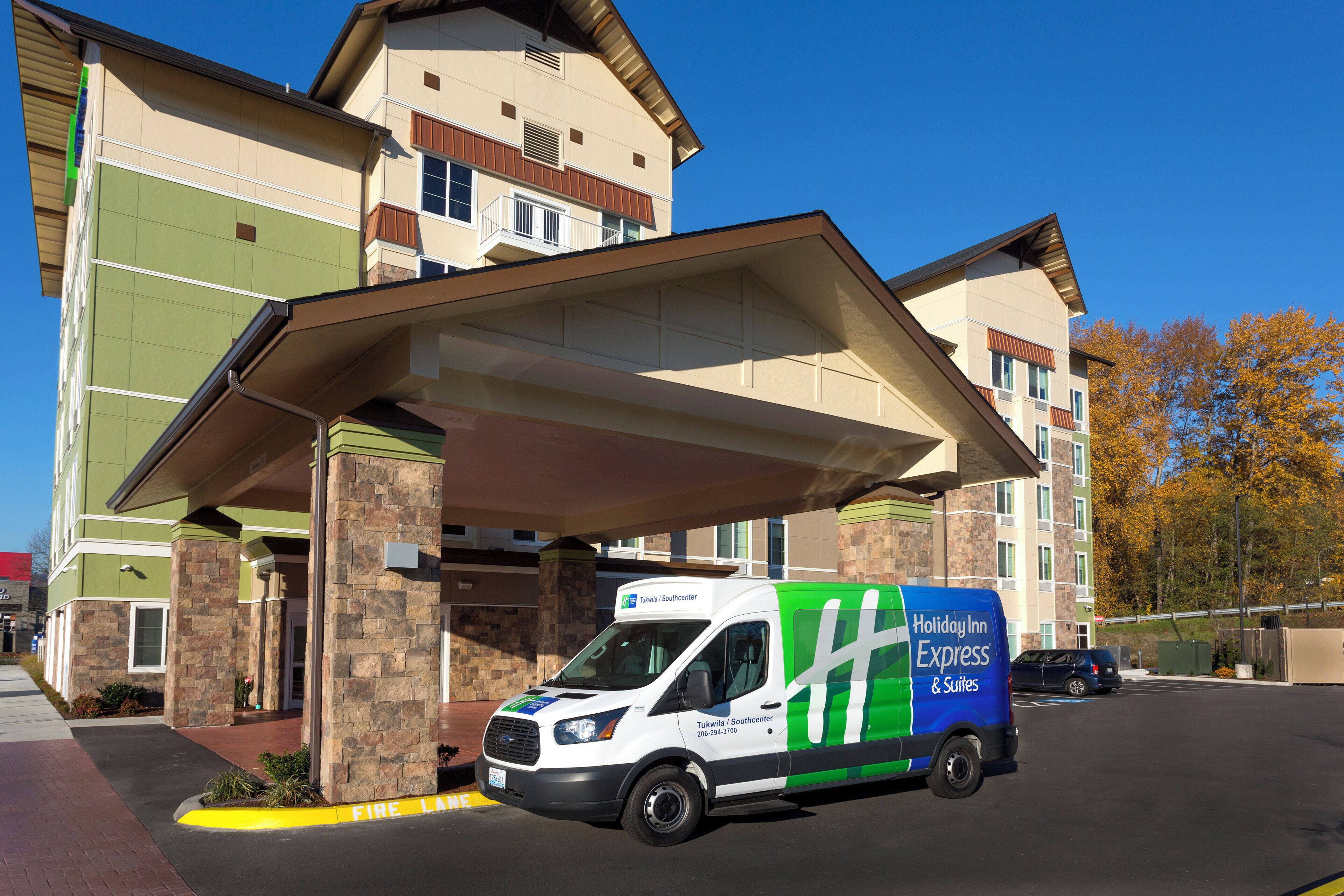 Uma van Holiday Inn Express & Suites estacionada em frente a um edifício com entrada coberta e pilares de pedra.