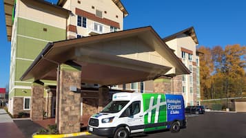 Uma van Holiday Inn Express & Suites estacionada em frente a um edifício com entrada coberta e pilares de pedra.