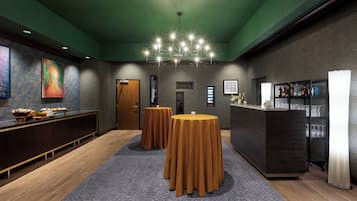 Um hall de hotel moderno com uma mesa de recepção, duas mesas redondas, um candelabro e um espaço de bar.