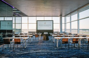 Uma sala de conferências com uma tela grande exibindo o logotipo da InterContinental Hotels & Resorts, mesas, cadeiras e piso coberto de carpete.