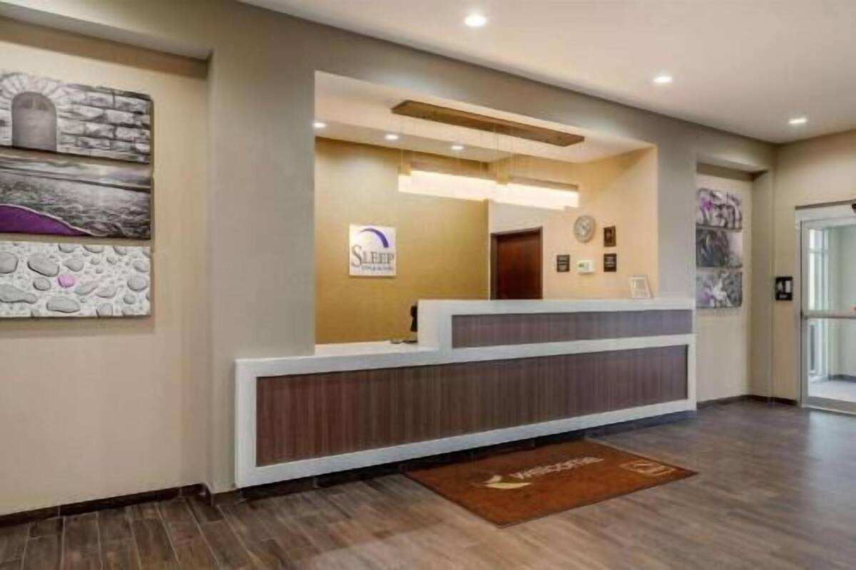 Uma área de recepção com um painel artístico de pedra, um balcão de recepção e um relógio na parede.