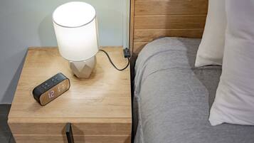 Uma mesa de cabeceira de madeira com uma lâmpada, um controle remoto e uma cama com almofadas.