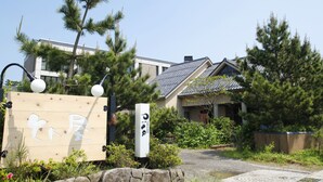 Um edifício japonês tradicional com telhado inclinado, rodeado por pinheiros e um caminho de pedra.