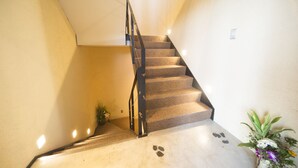 Uma escada com corrimão, degraus carpetados e luminária fixada na parede.