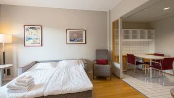 Quarto de hotel com cama, uma cadeira, uma mesa e duas imagens emolduradas na parede.