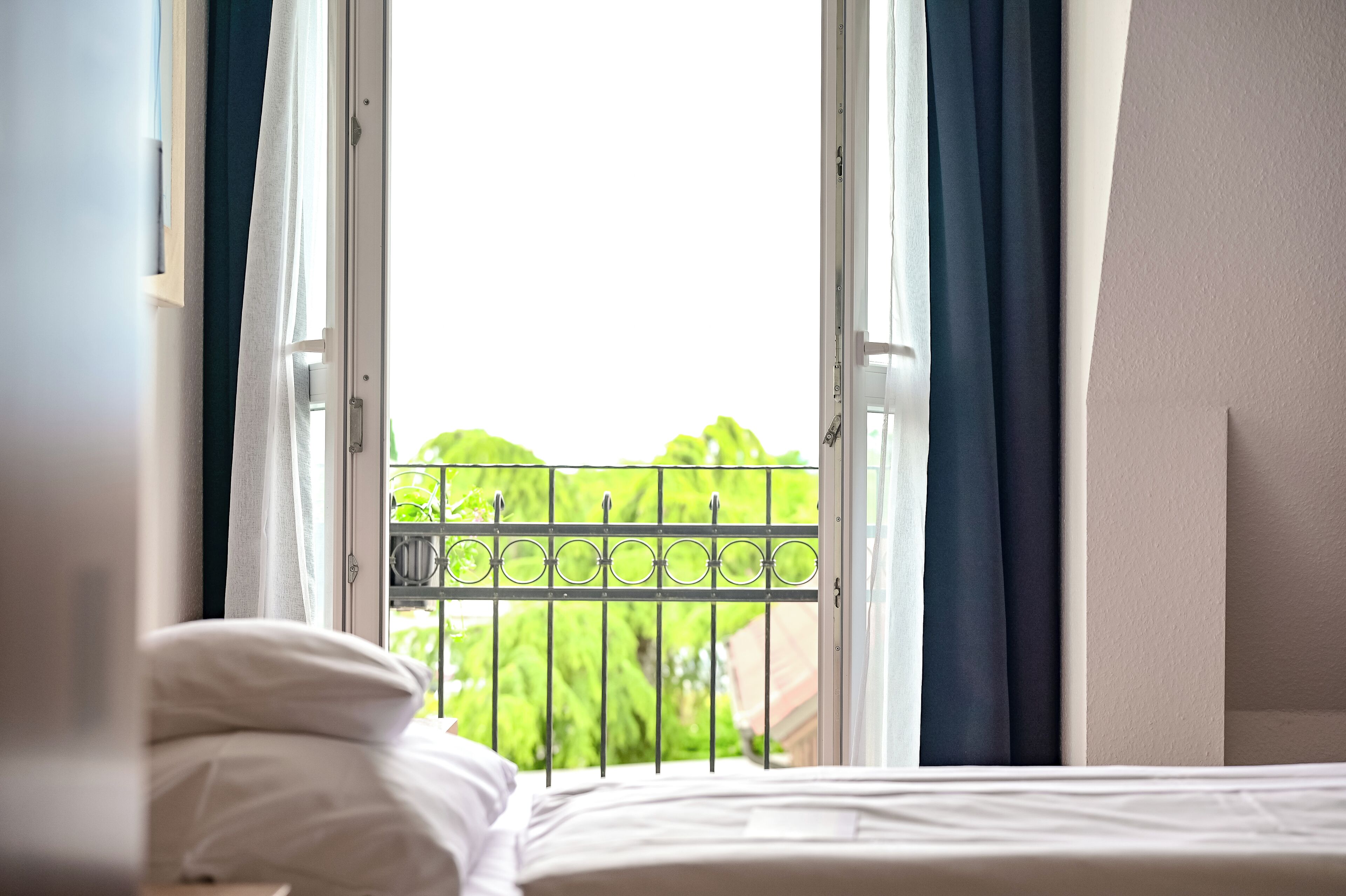 Quarto de hotel com cama, janela e vista para área verde, além de grade de metal.