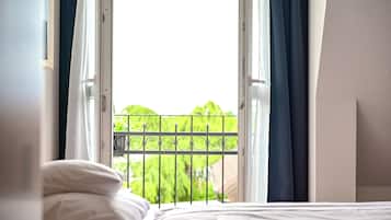 Quarto de hotel com cama, janela e vista para área verde, além de grade de metal.
