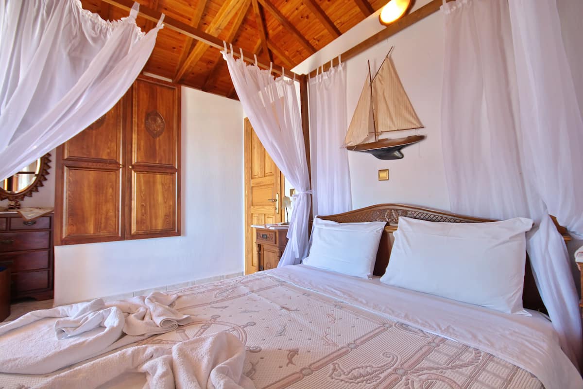 Quarto com teto de madeira, cama com roupa de cama branca e decoração de veleiro na parede.
