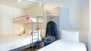 Quarto de hotel com beliches, cabideiro suspenso, mala e prateleira fixada na parede.