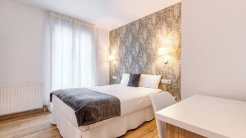 Quarto com cama, luminárias laterais, radiador e chão de madeira.