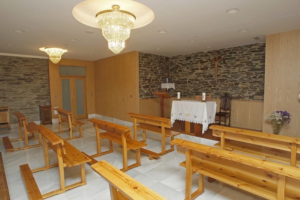 Interior de igreja com bancos de madeira, parede de pedra, altar de madeira e um candelabro.