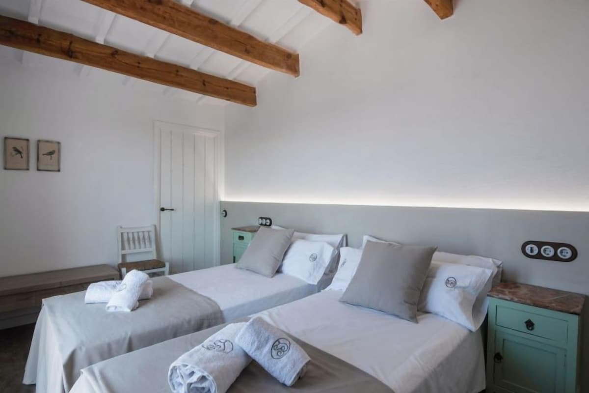 Quarto com duas camas, teto de madeira, porta branca e um pequeno armário verde.