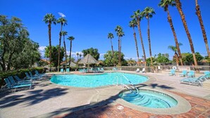 Piscina com espreguiçadeiras, palmeiras e um gazebo.