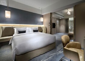 Quarto de hotel com uma cama grande, mesa de cabeceira, cadeira, espelho e guarda-roupa.
