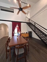 Uma área de refeições com mesa e cadeiras de madeira, um ventilador de teto e uma escada.