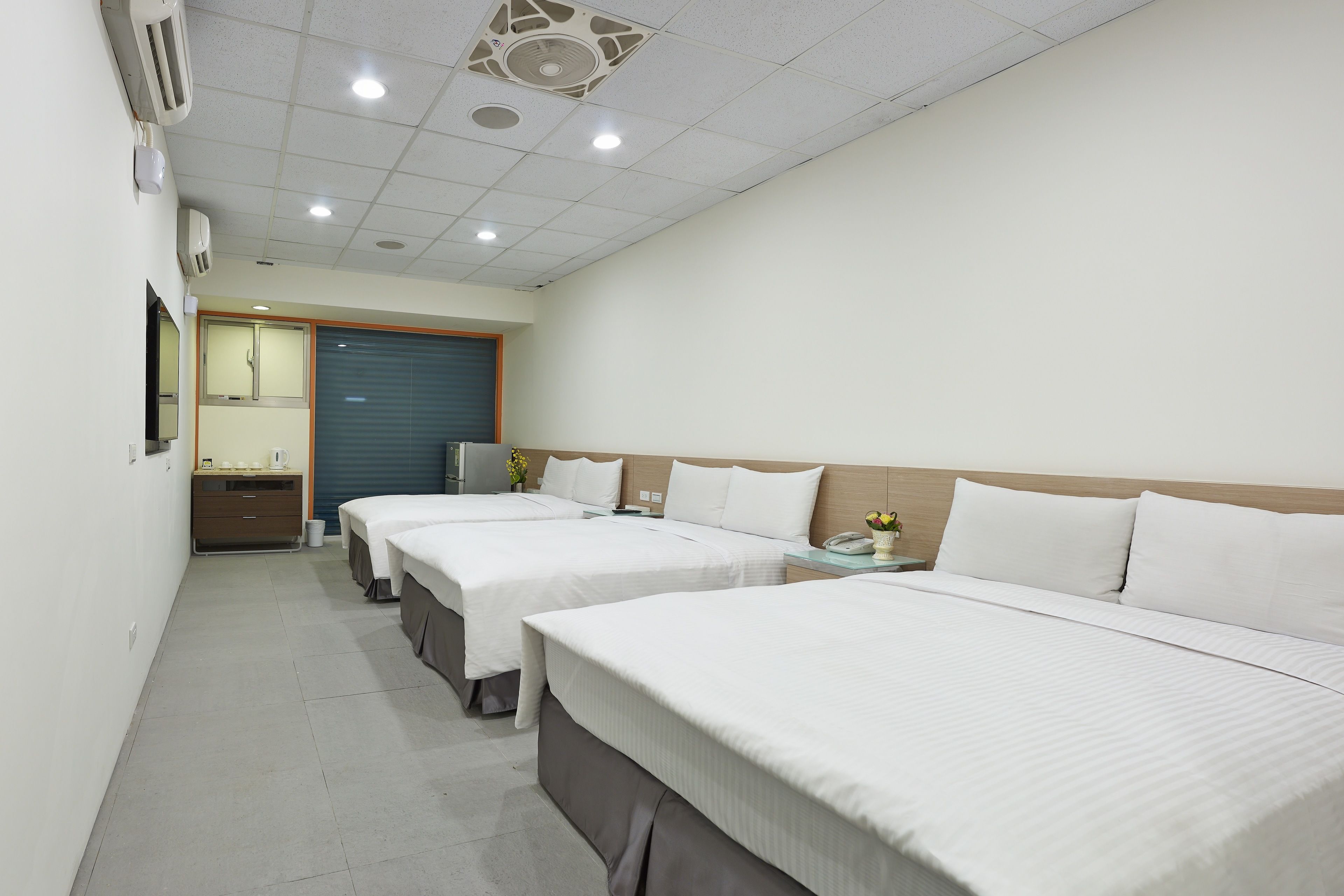 Quarto de hotel com duas camas de solteiro, uma pequena escrivaninha com abajur e uma janela com vista para o exterior.
