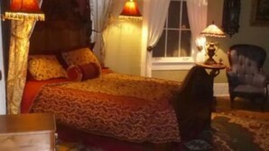 Quarto com cama, cadeira, abajur e janela.