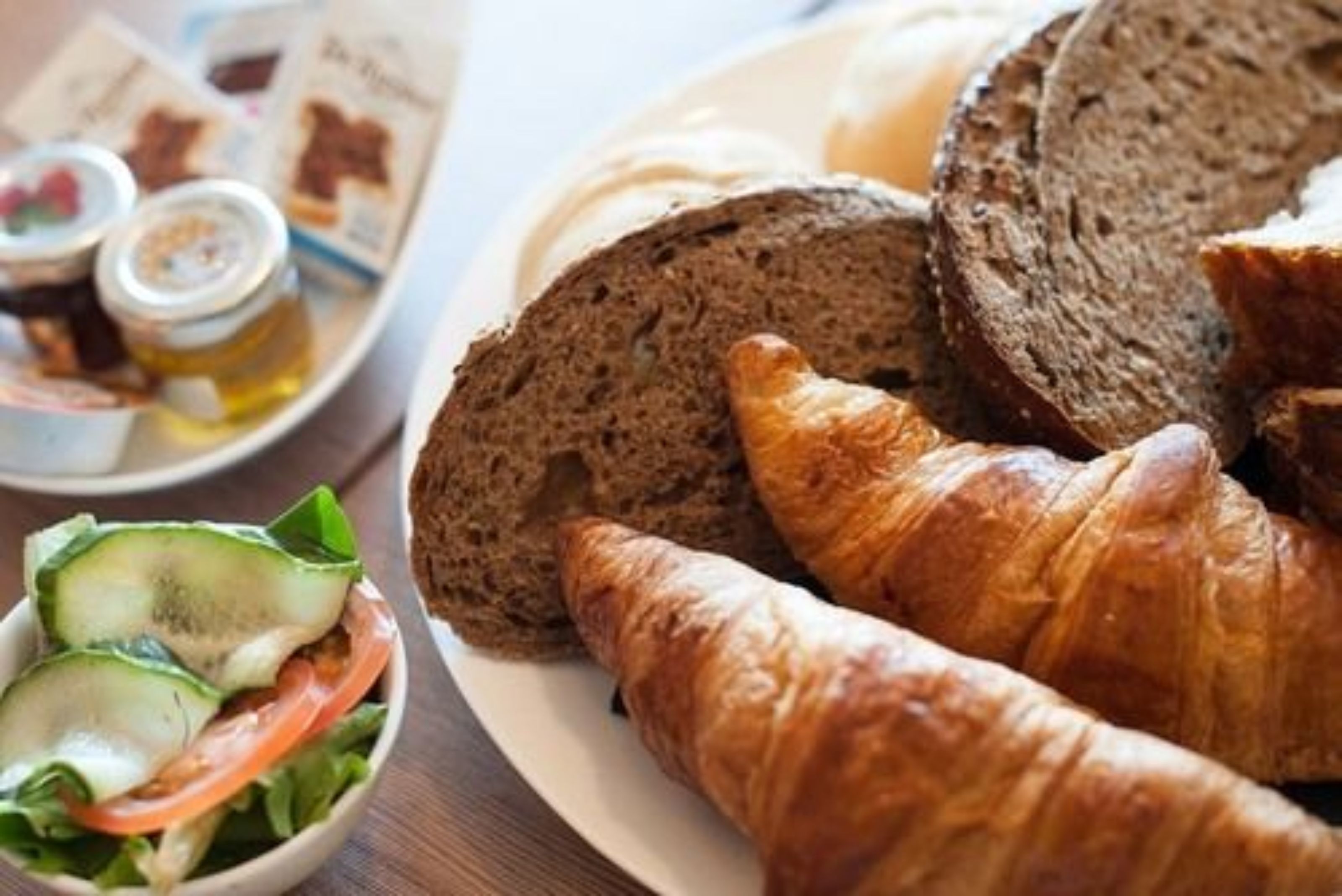 Um prato com fatias de pão integral, um croissant e uma salada pequena com alface e tomate.