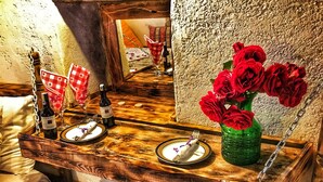 Uma toucador de madeira com um espelho, um vaso verde com rosas vermelhas, uma garrafa de vinho e um tecido xadrez.