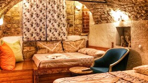 Um quarto rústico com teto abobadado, uma cama com roupa de cama estampada, uma cadeira azul e uma pequena mesa.