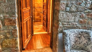 Um corredor estreito com portas de madeira que dão para um banheiro com chuveiro e parede revestida de azulejos.