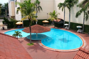 Piscina cercada por palmeiras, espreguiçadeiras e guarda-sóis.