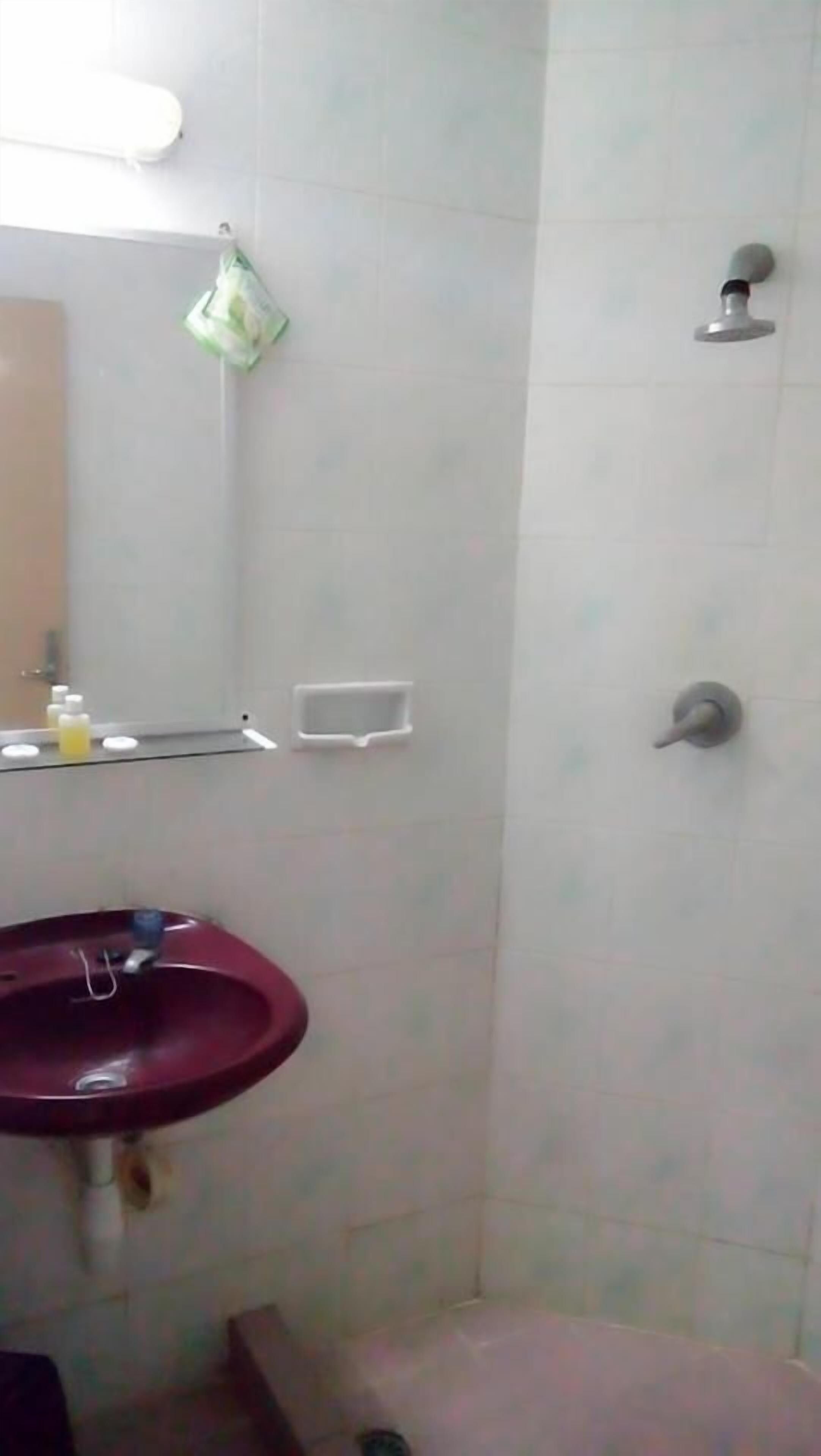 Casa de banho com uma pia vermelha, espelho, chuveiro e suporte para toalhas.