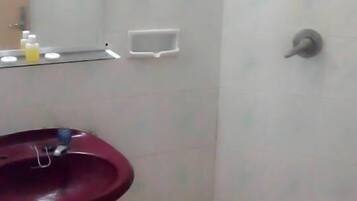 Casa de banho com uma pia vermelha, espelho, chuveiro e suporte para toalhas.