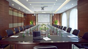 Uma sala de conferências com uma mesa comprida, cadeiras, laptops e garrafas de água.