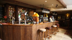 Uma área de bar com banquetas de madeira, diversos frascos e uma torneira de chopp grande.