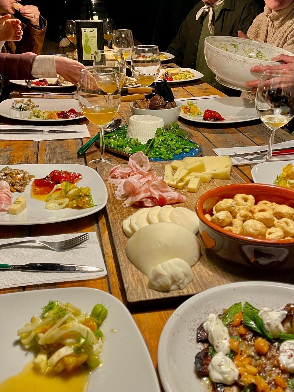 Uma mesa de jantar com diversos pratos, incluindo queijo, carnes e vegetais, além de várias taças de vinho.