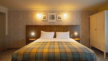 Quarto de hotel com cabeceira de madeira, duas luminárias de cabeceira, colcha xadrez e papel de parede estampado.