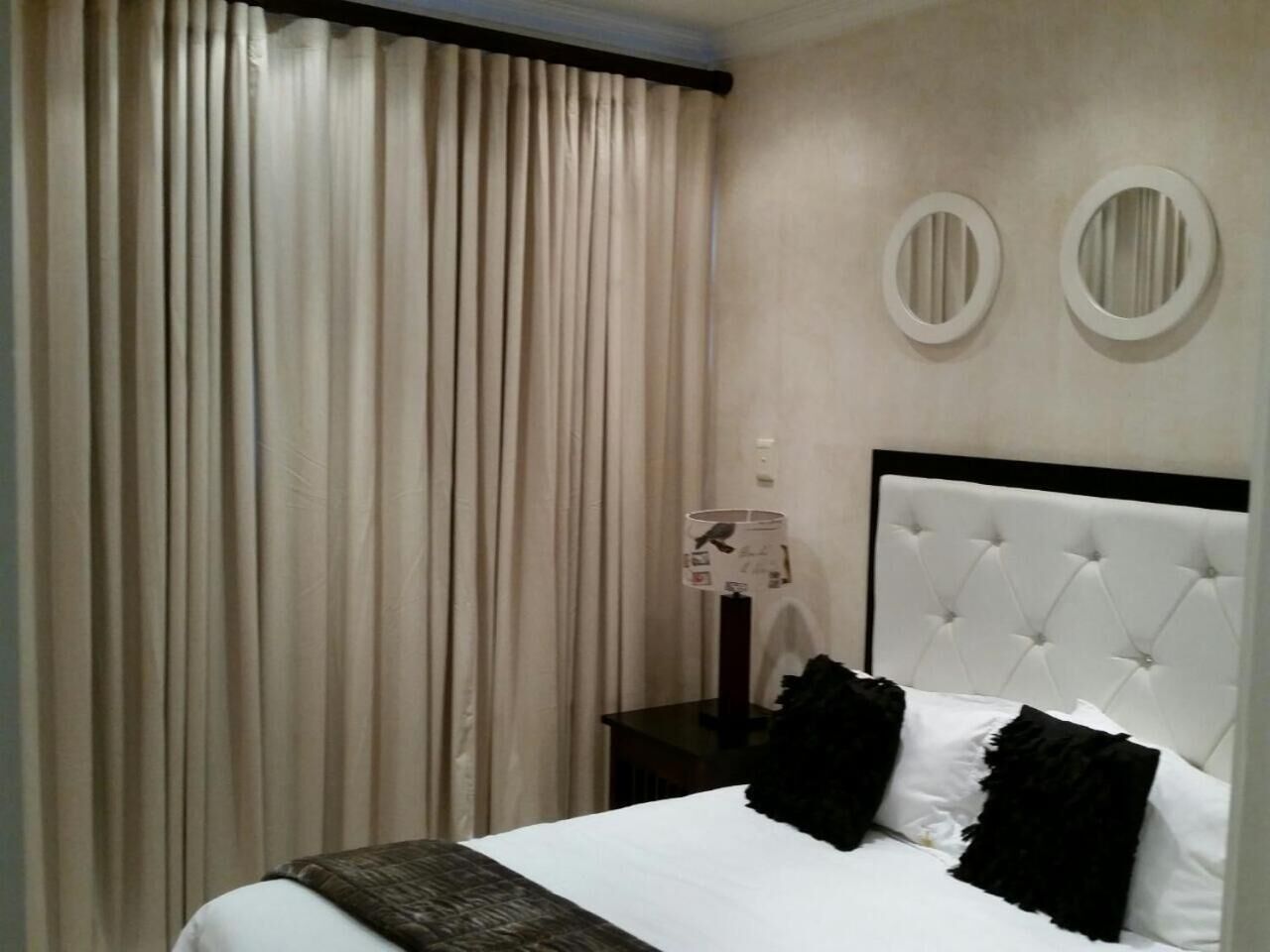 Quarto de hotel com uma cama grande, uma mesa de cabeceira, um abajur e uma janela com cortinas.