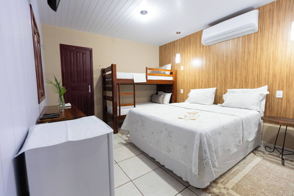Quarto com uma cama beliche, escrivaninha, cadeira, porta e ar condicionado.