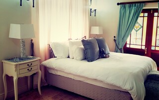 Quarto com cama, duas mesas de cabeceira, abajur e janela com cortinas.