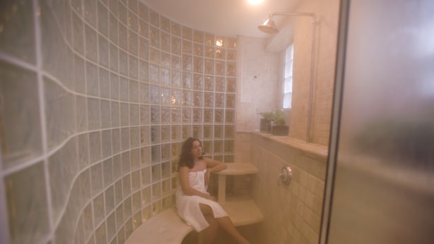 Casa de banho com parede revestida de azulejos de vidro, uma pia e zona de duche.